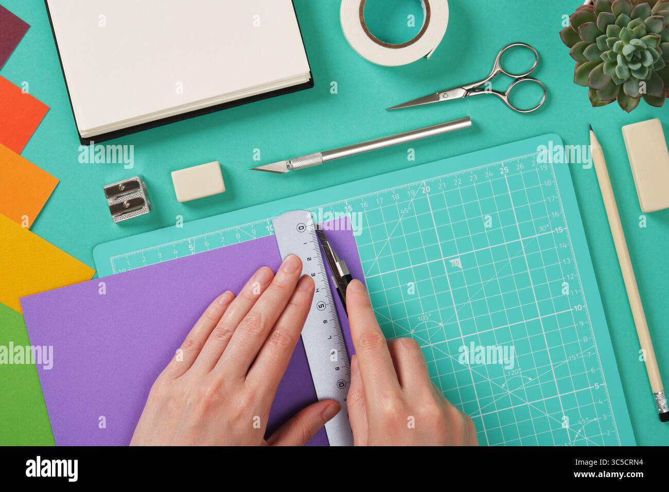 Hands working with colorful paper using a paper knife on mint green ...