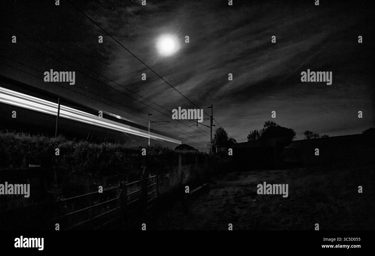 A black & white image of a train passing in the night inder moonlight ...