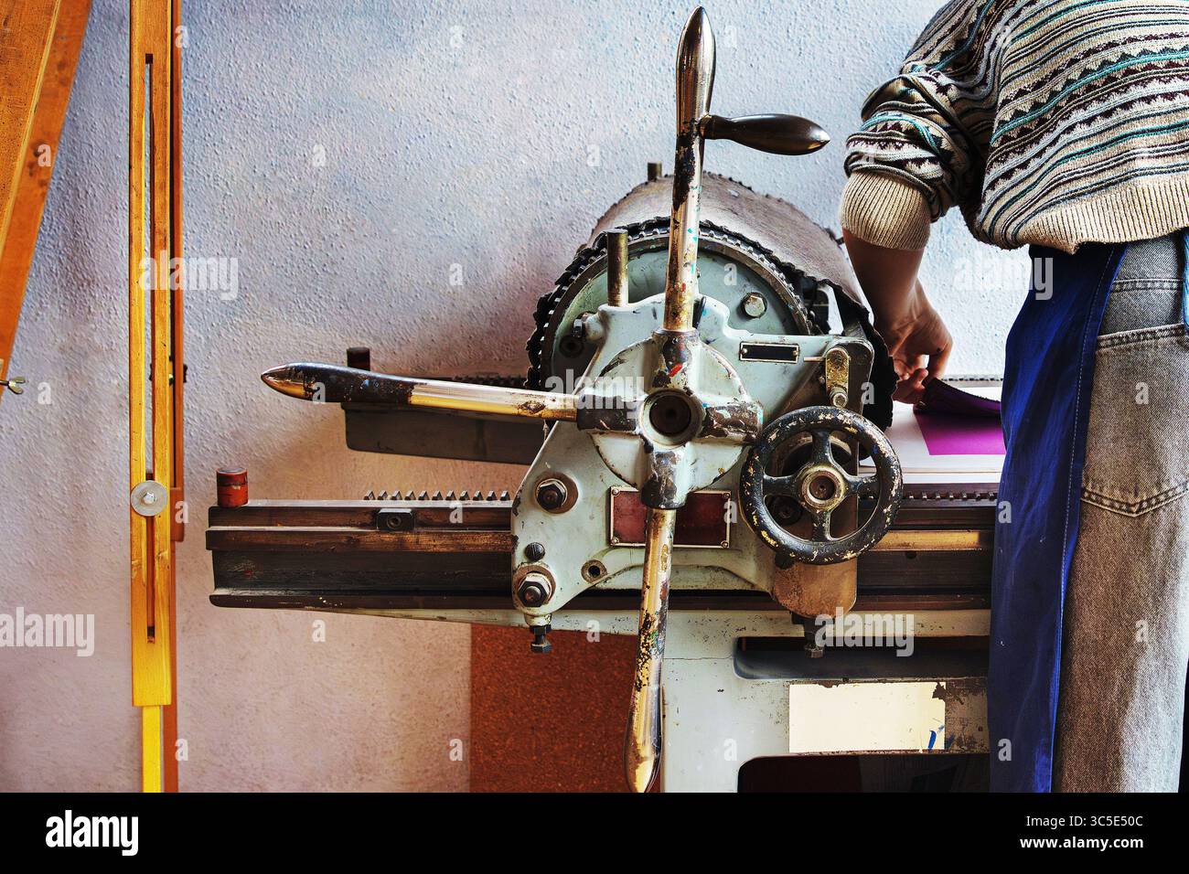 A printmaker in a patterned sweater and apron operates a traditional ...