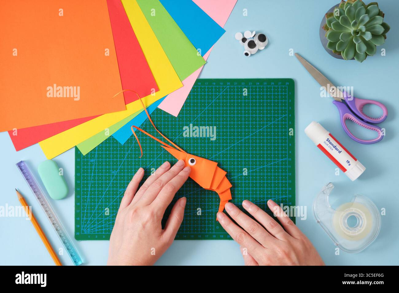 Making origami shrimp from orange paper. Female hands against a green ...