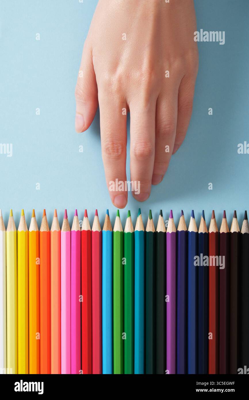 Hand choosing green colored pencil from a row of multi-colored pencils ...