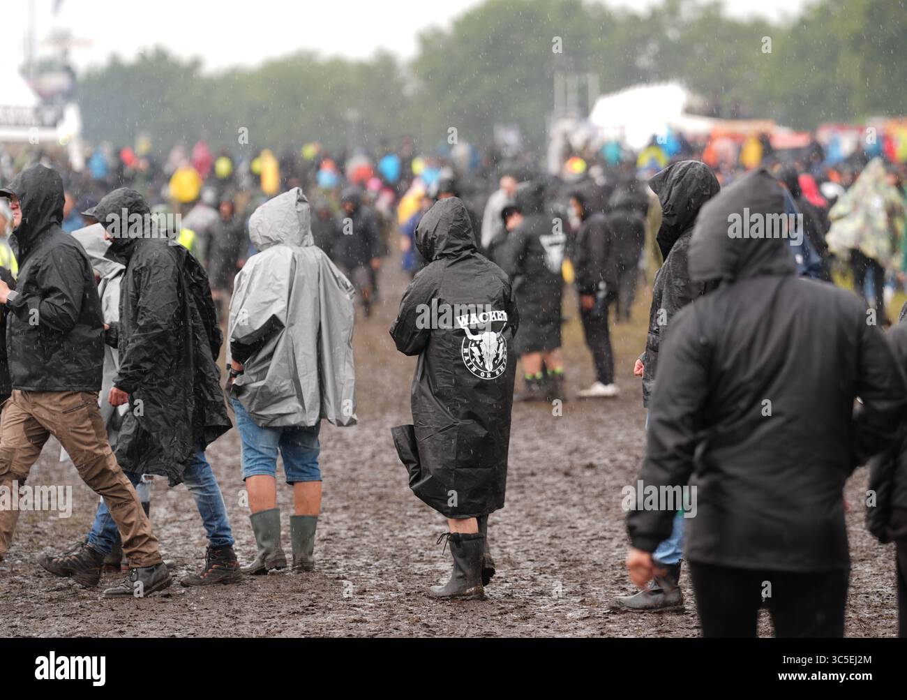 Wacken, Germany. 30th July, 2025. Metal fans walk through the mud at ...