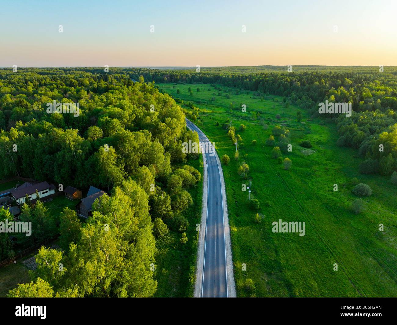 An aerial view shows a winding road cutting through a vast expanse of lush green forest and open ...