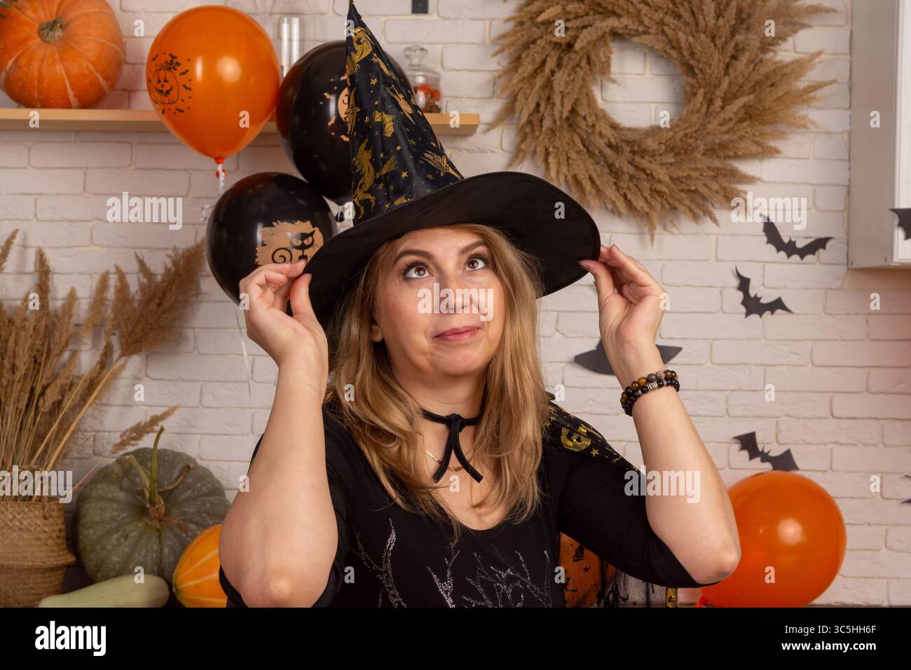 A beautiful woman in a black dress puts on a witch hat on a background ...