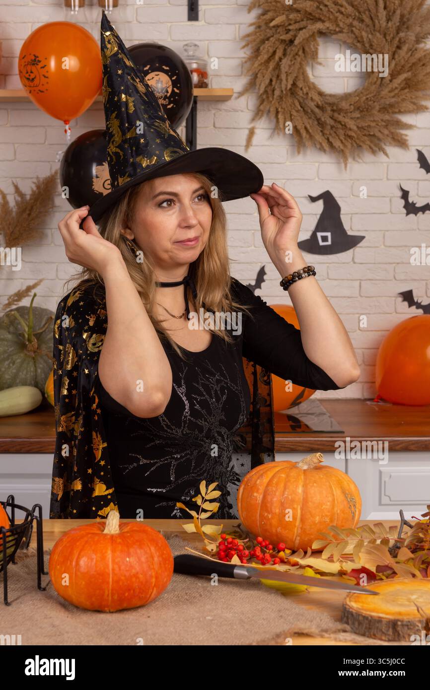 A beautiful woman in a black dress puts on a witch hat on a background ...