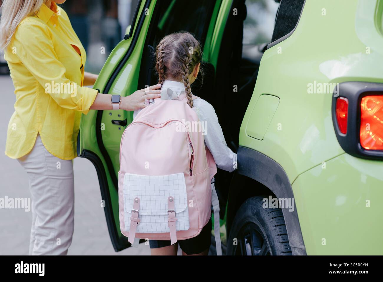 Mother helps daughter get into car for the school run, showing family ...
