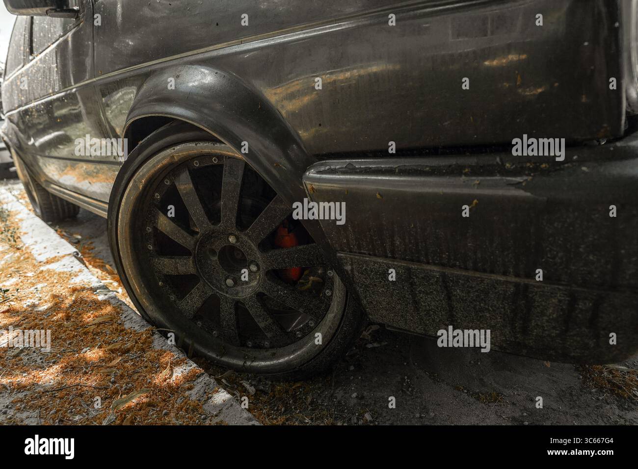 Close-up of a flat rear tire on a dirty, dented black car parked on a ...