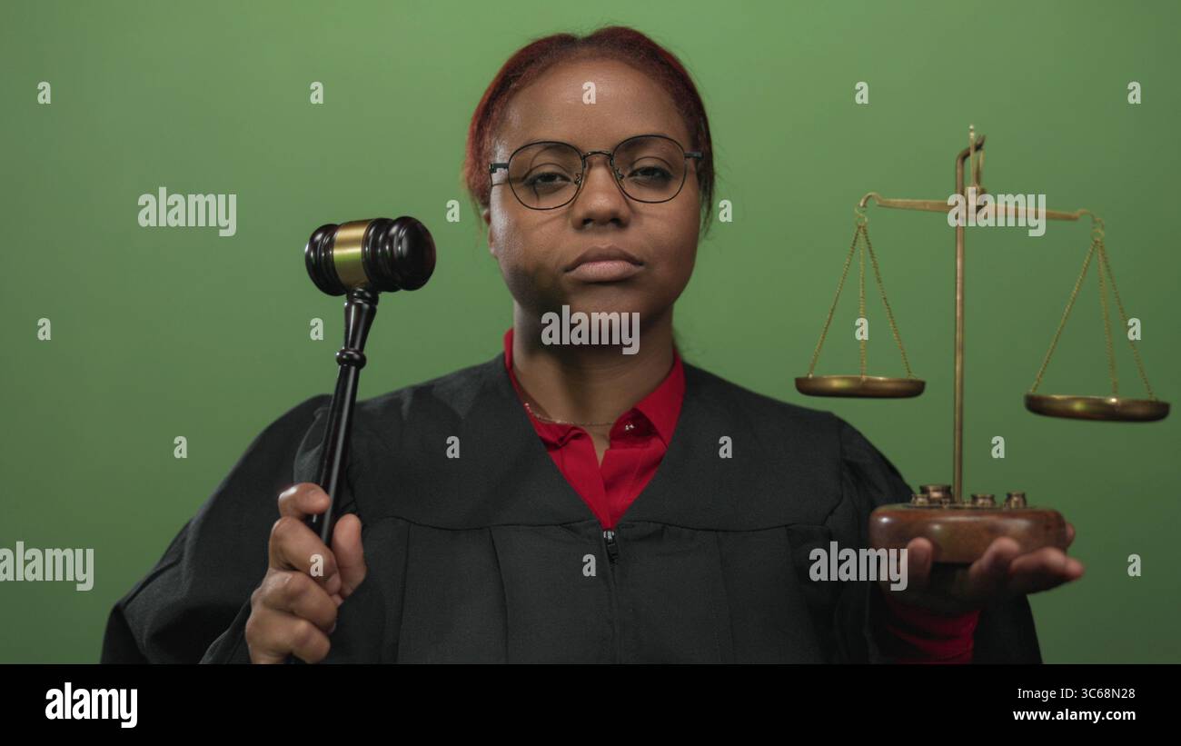 Serious african american judge holds gavel and scales in green studio ...