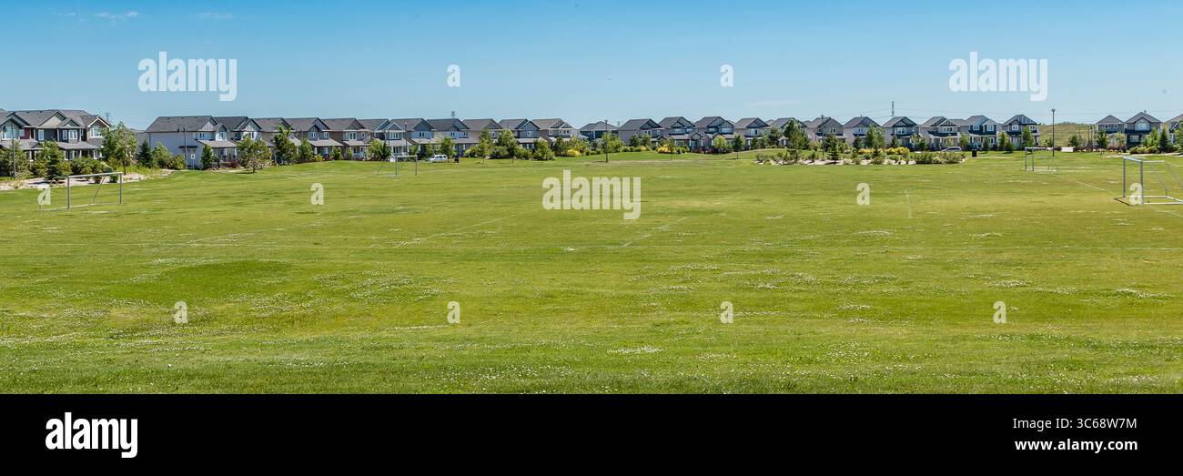 Large, grassy field with a few houses in the background. The houses are ...