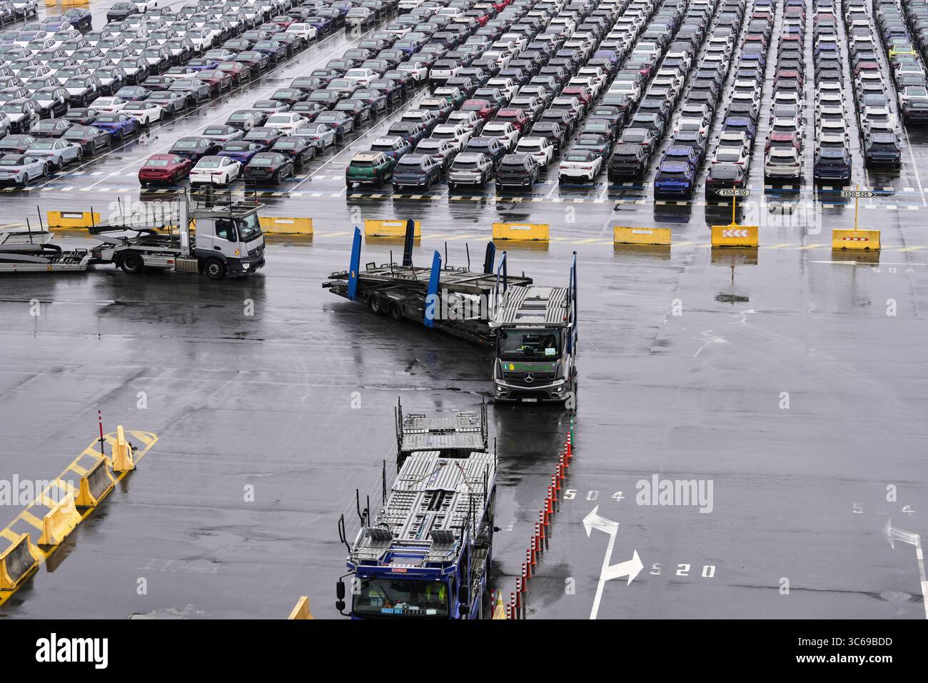 Car carriers drive past new cars parked in a lot at the International ...
