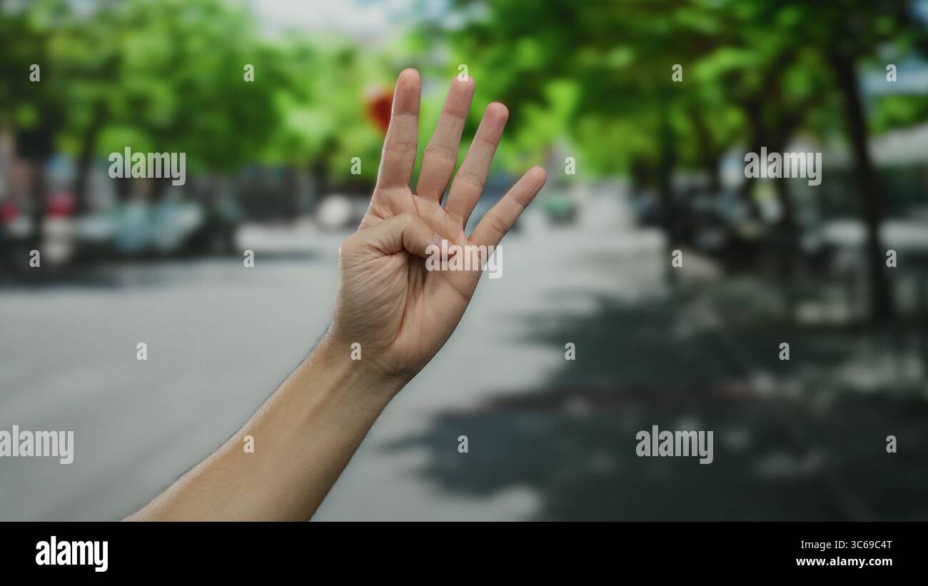 Man's hand showing four fingers in a bright city street with green ...