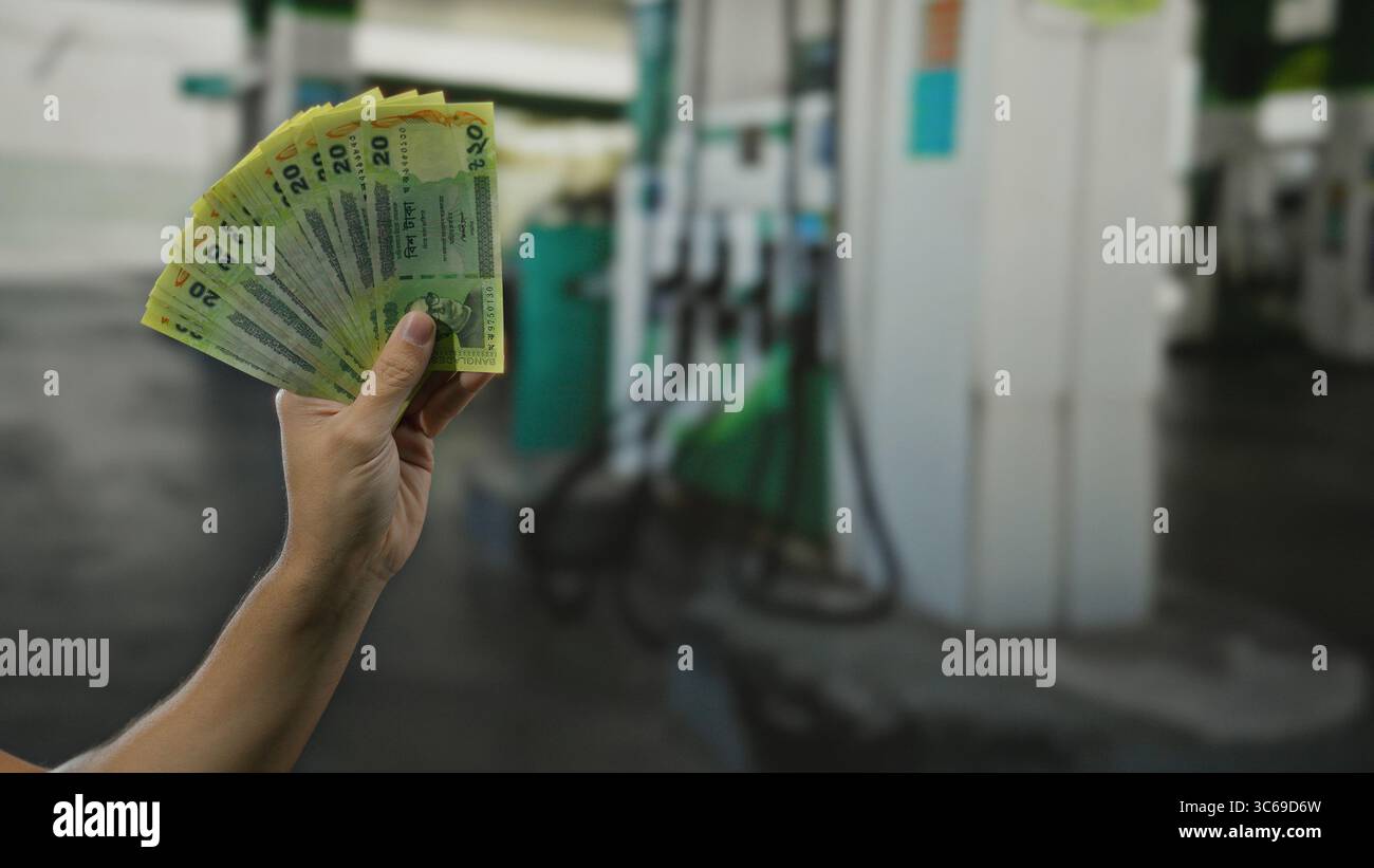 Man holding bangladeshi taka notes at an outdoor petrol station ...