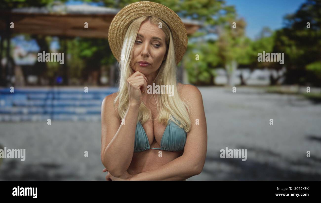 Woman in straw hat wearing bikini top bares chest while looking down in forest; quiet ...