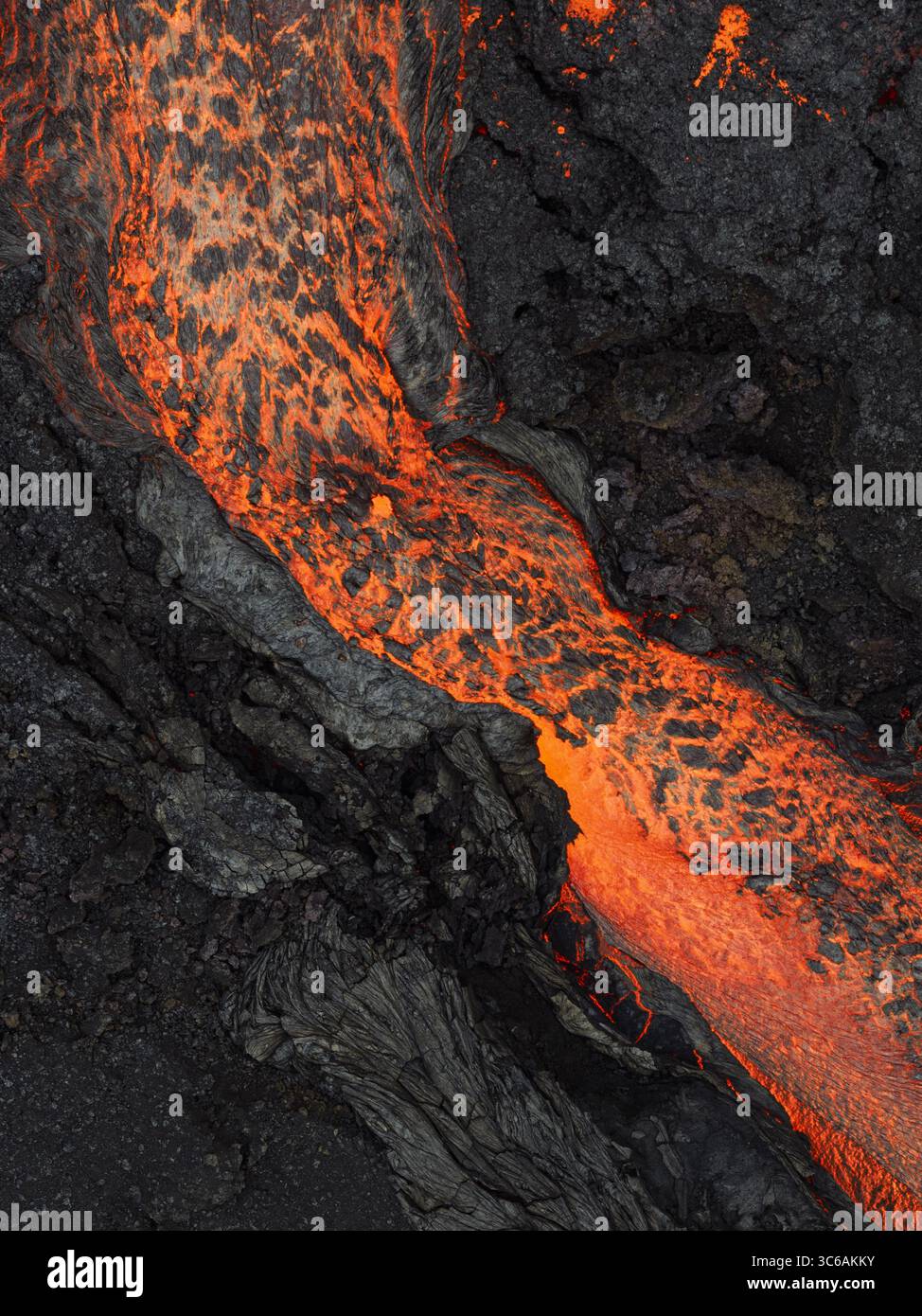 Aerial view of molten lava snaking through rugged, blackened earth, a fiery river cutting ...