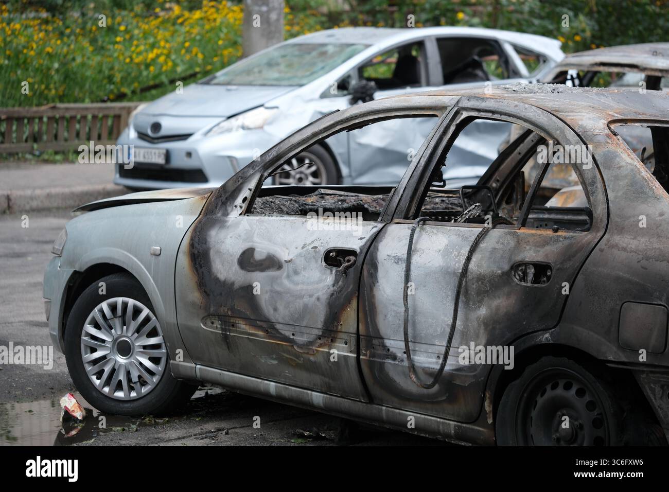 Damaged and burned vehicles line the street in a somber urban setting ...