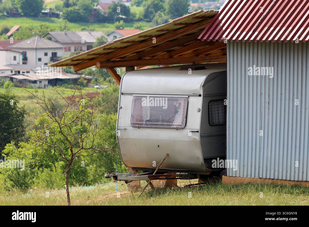 An aging gray caravan is partially enclosed by a rough shed made with a ...