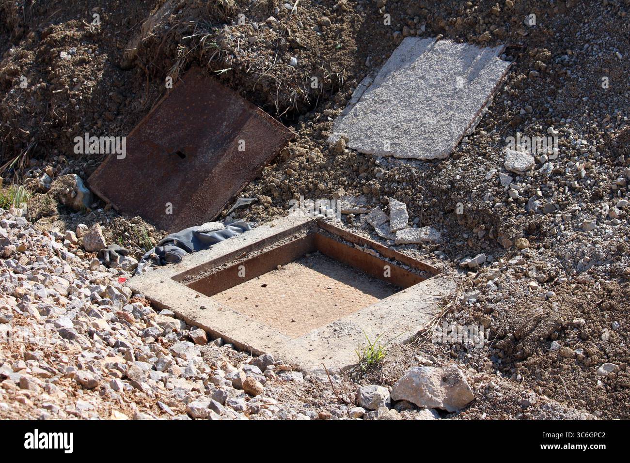 A partially buried square concrete utility chamber lies open with its ...