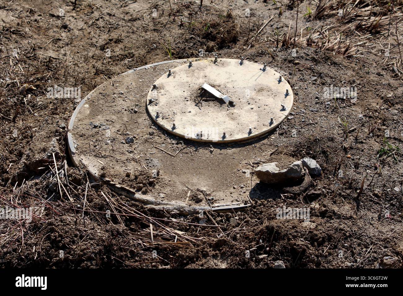 A heavy concrete manhole cover with metallic bolts and a handle is ...