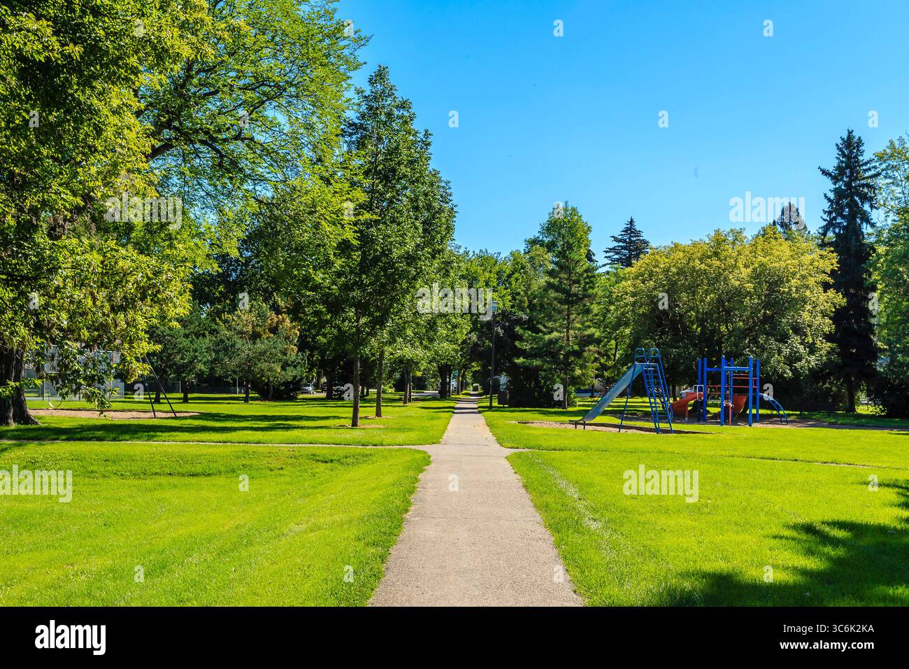 Park with a path and a playground. The path is paved and the playground ...