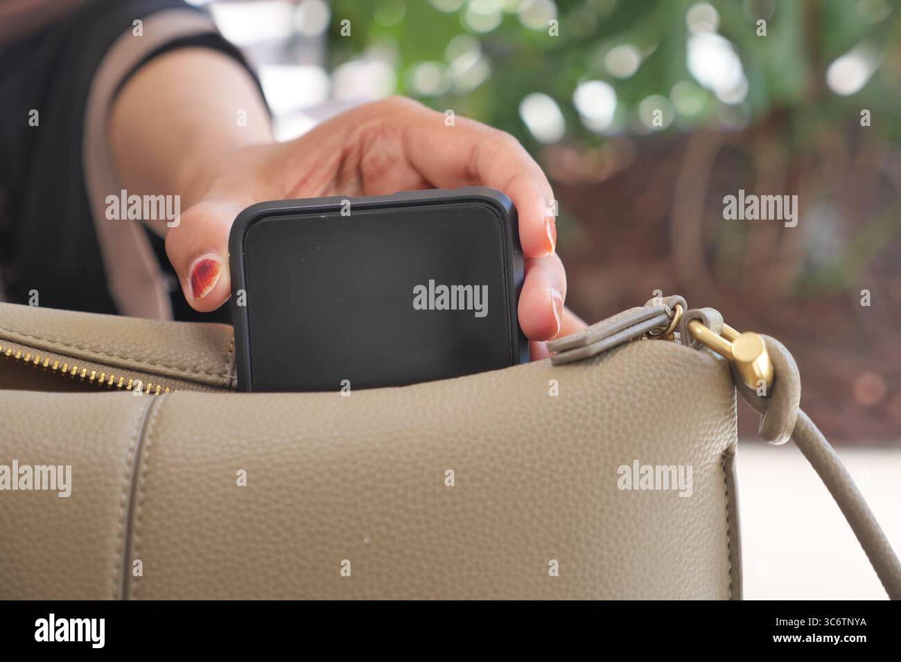 Hand placing smartphone into handbag Stock Photo - Alamy