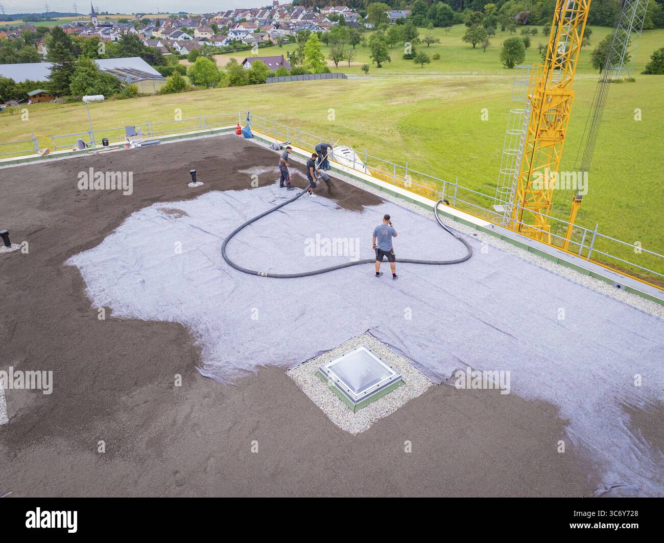 Workers attaching hoses to a roof next to an open field, roof greening ...
