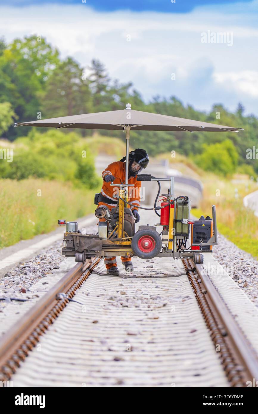 Worker using a machine on railway tracks under an umbrella, surrounded ...