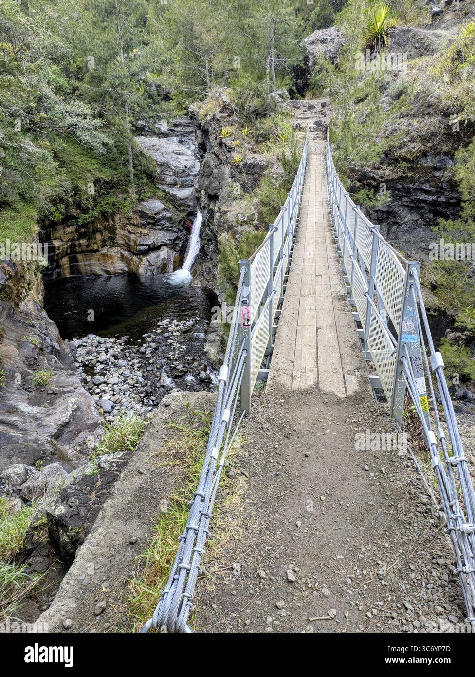 Metal footbridge crossing above a small waterfall in a rocky forested ...