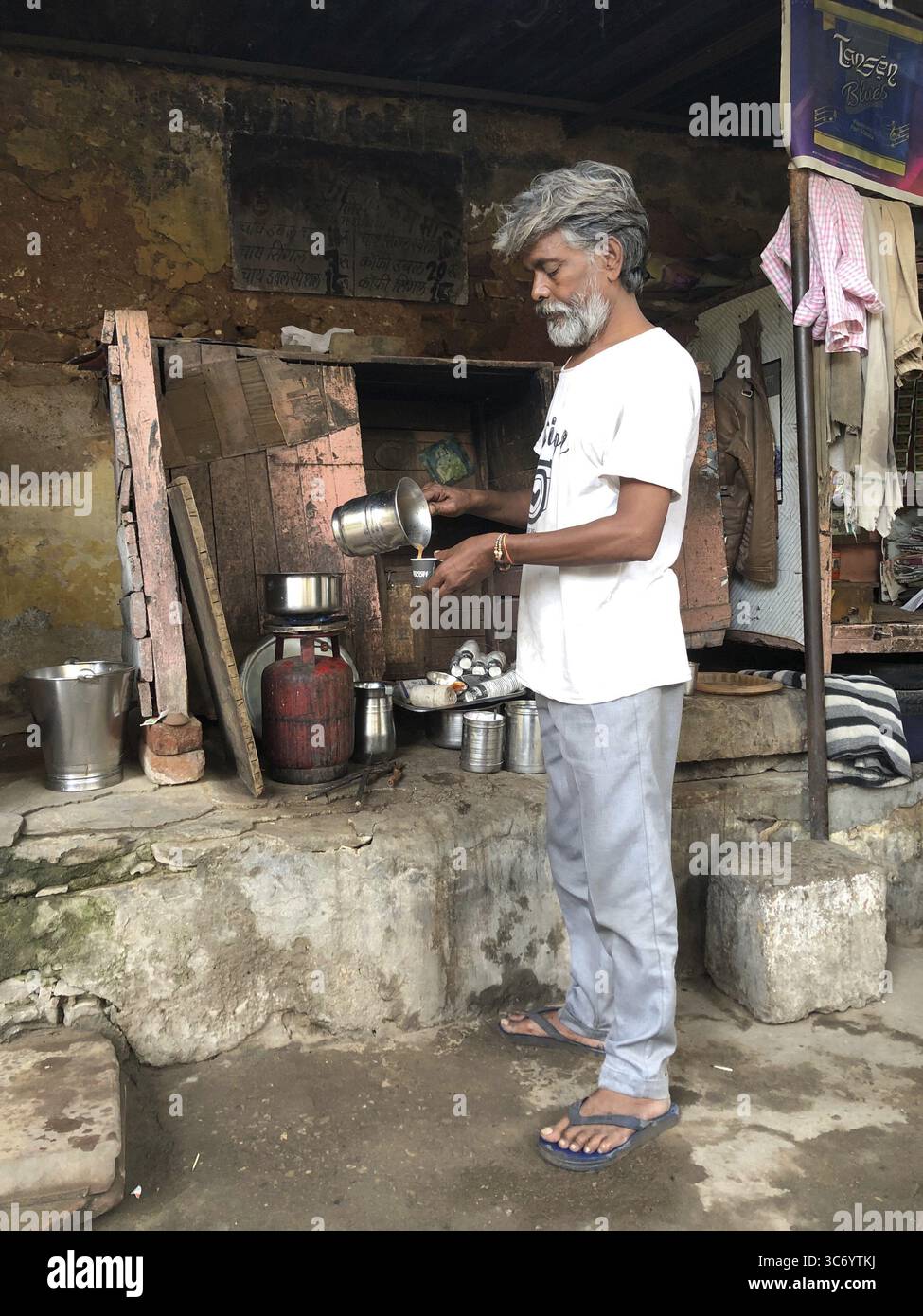 Man pouring chai in a makeshift street kitchen with pots and mugs ...