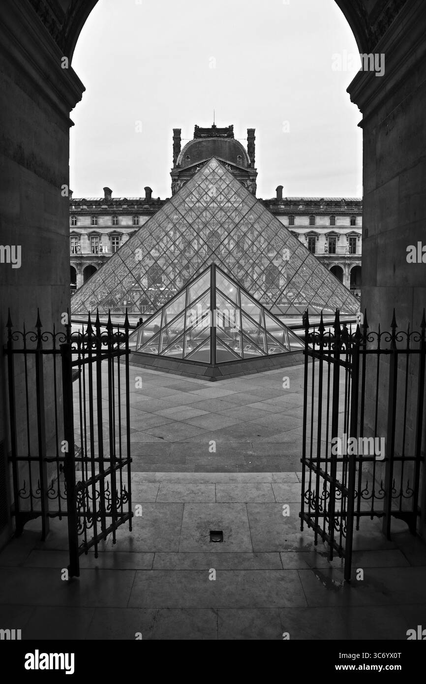 Daytime view of the Louvre Pyramid seen through an archway with ...