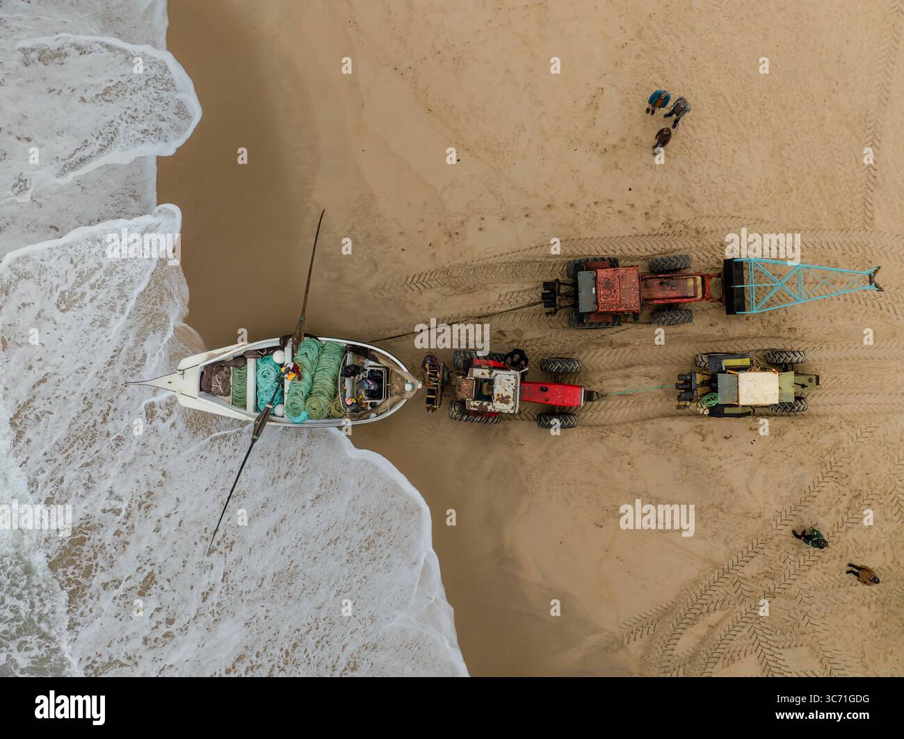 Aerial view of tractors on the beach pulling a fishing boat from the ...