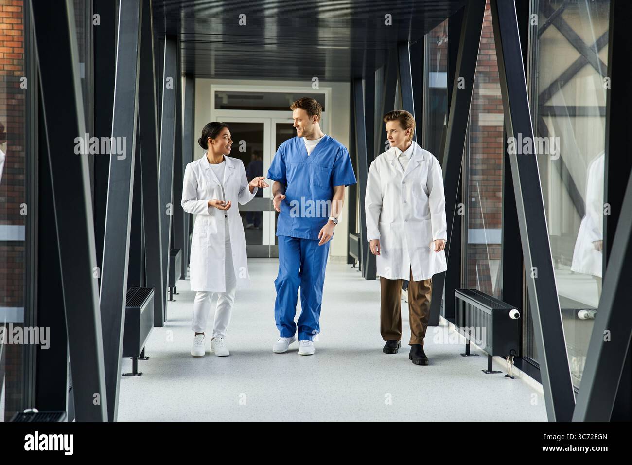 A Black woman and two doctors chat animatedly while walking down a ...