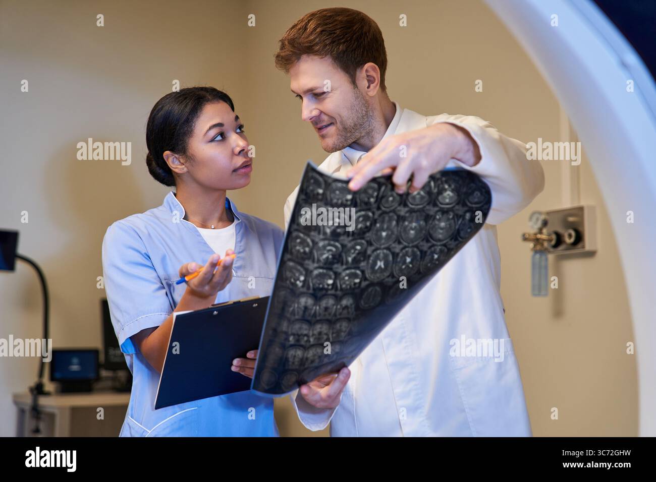 In a modern hospital, a man and woman in white coats examine an MRI ...