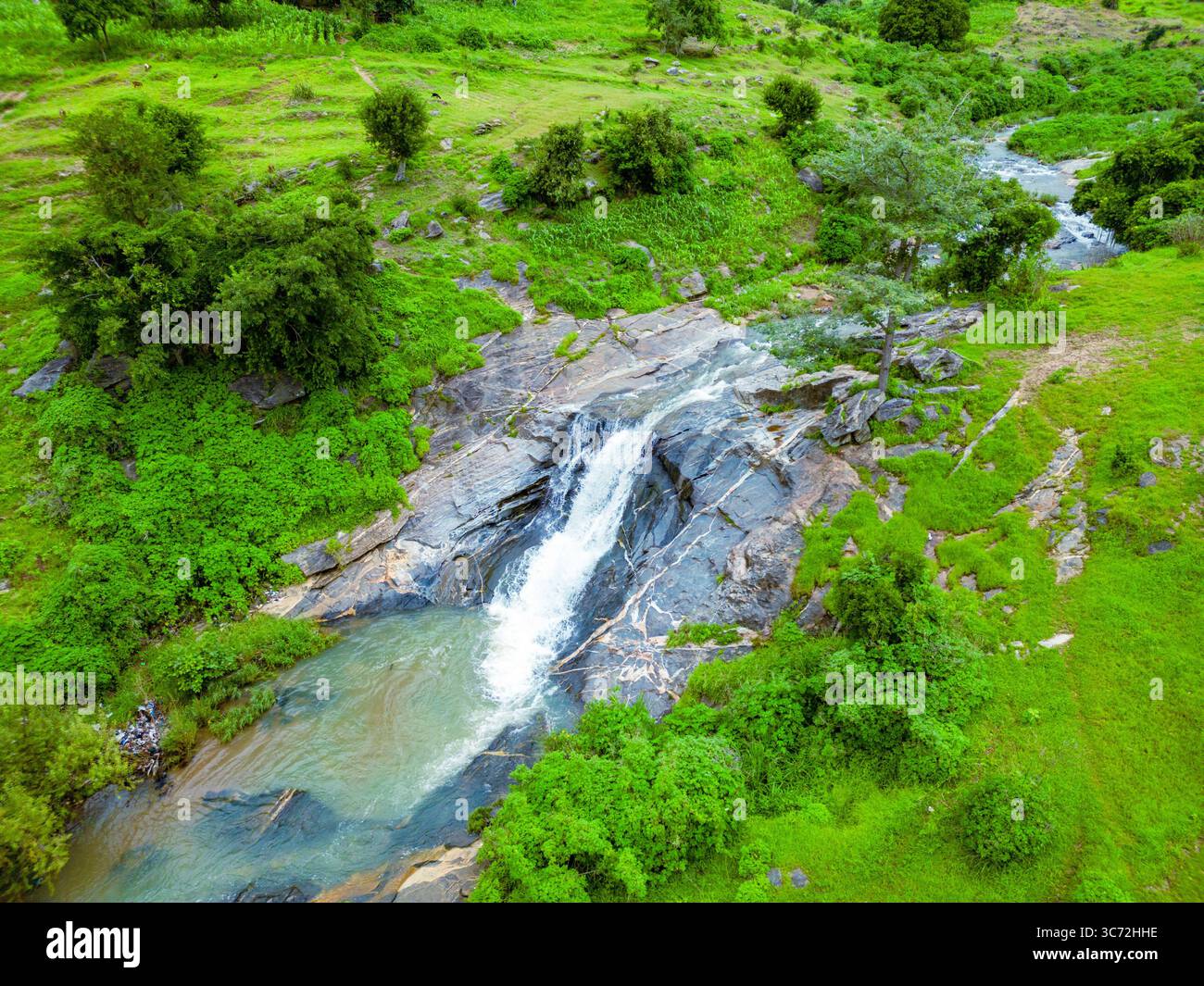 Aerial view of cascading waterfall over rugged rocks, embraced by ...