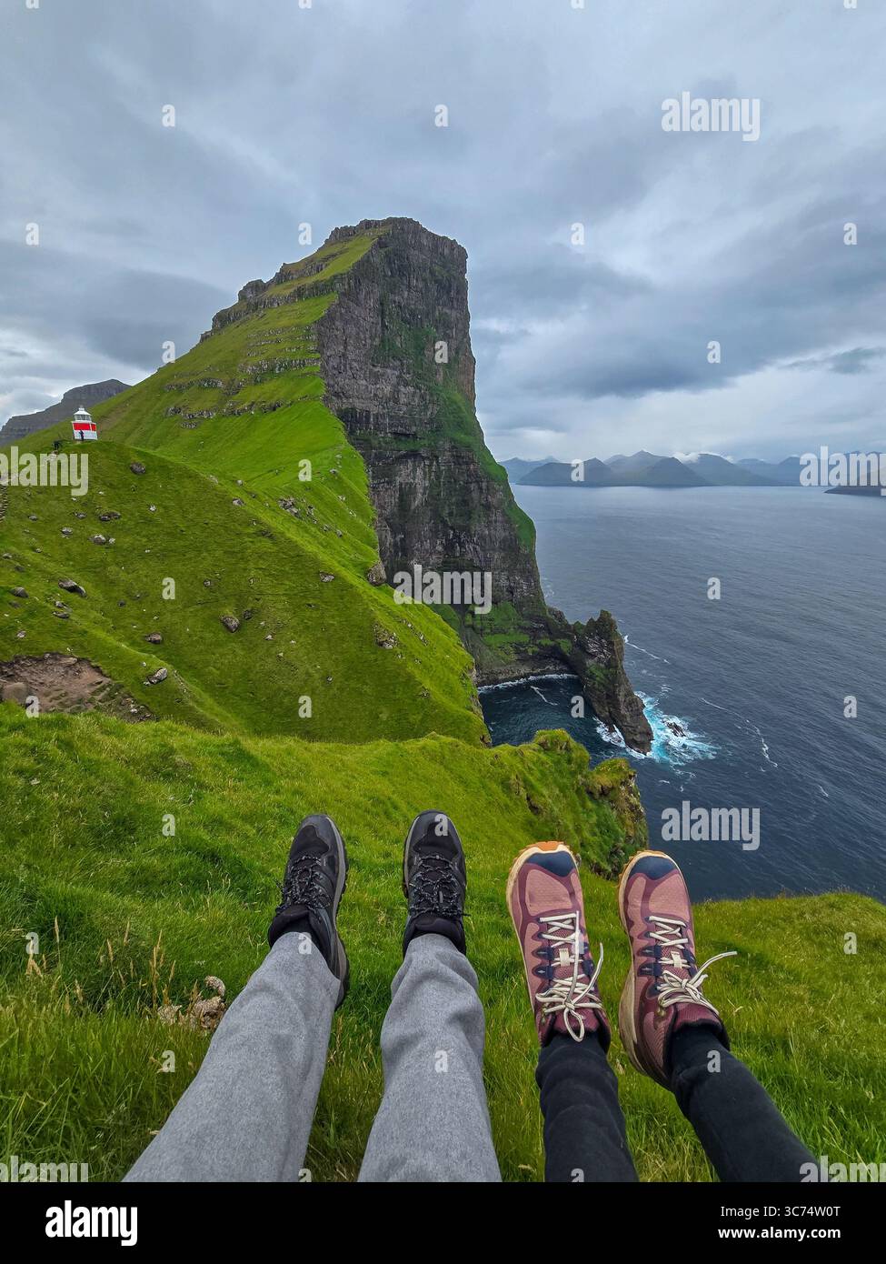 Two pairs of feet dangle over the edge of a lush green cliff in the ...