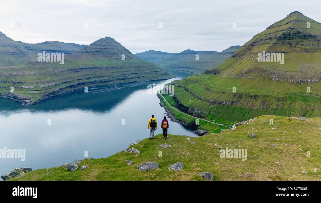 Two hikers stand at the edge of a stunning green valley, overlooking ...