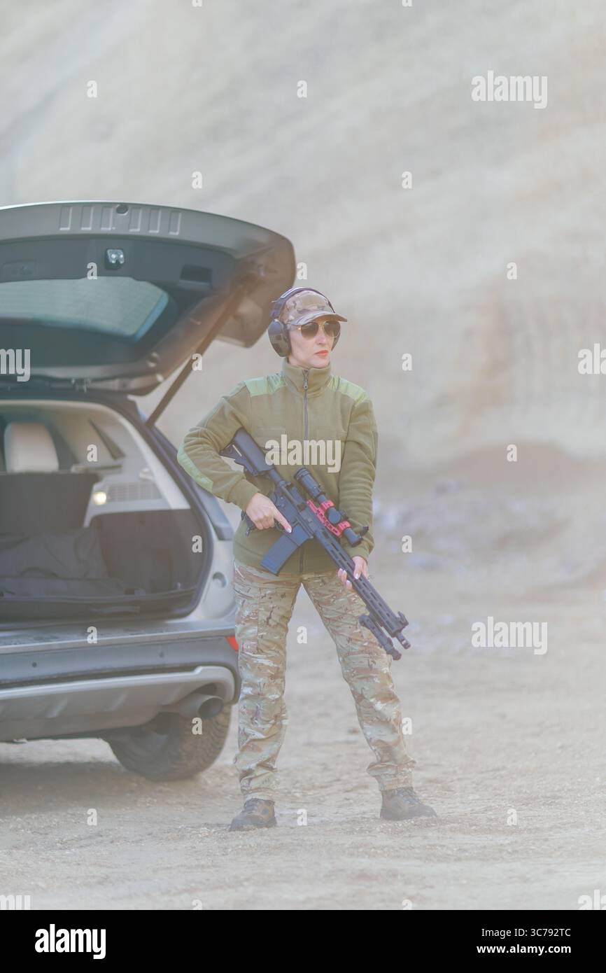 Female soldier standing near vehicle with open trunk, holding rifle ...