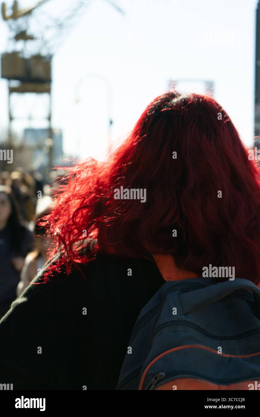 Woman with vibrant, flowing red hair walks down a bustling city street ...