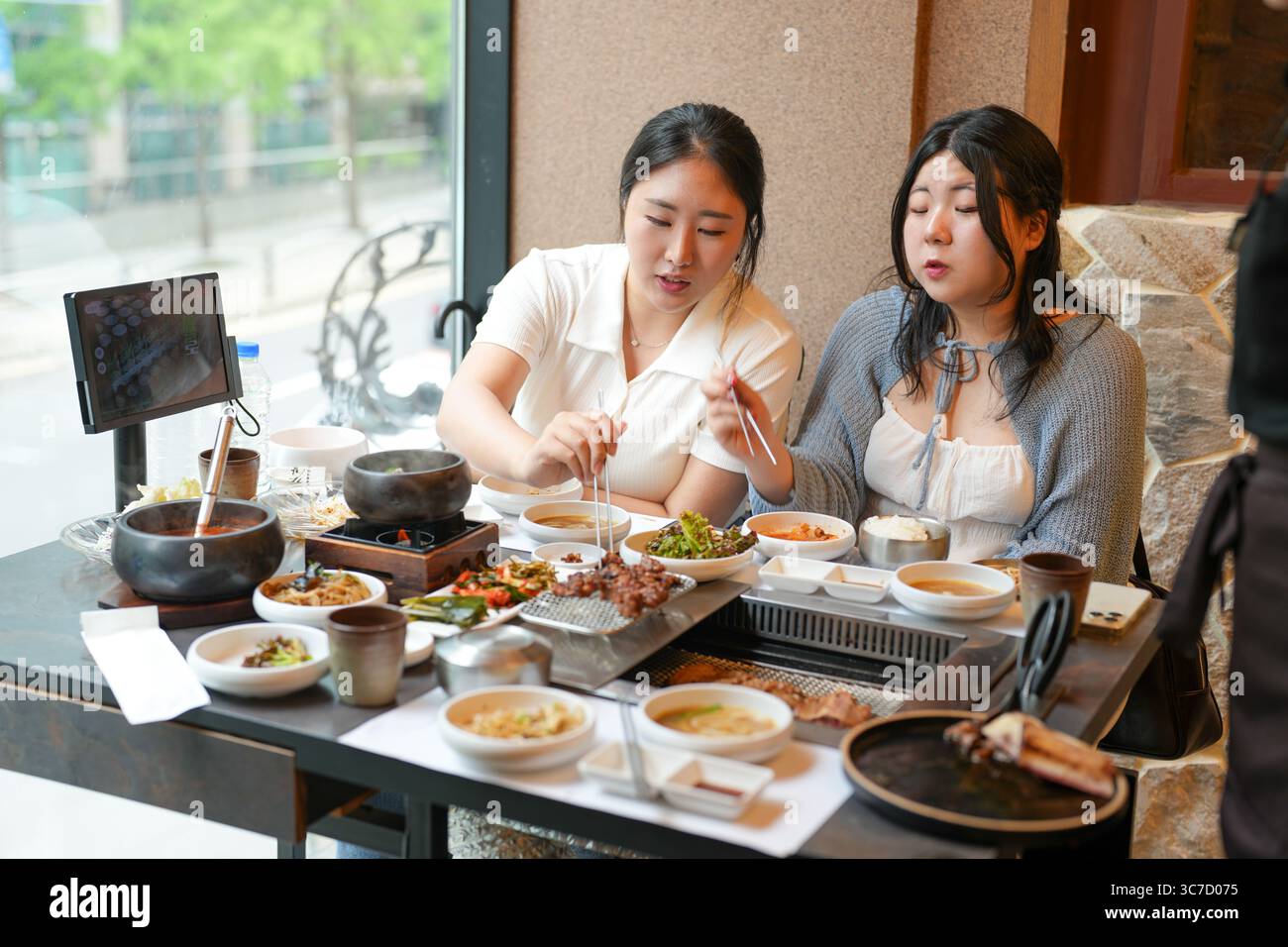 In a kalbi barbecue restaurant at a sunlit window table, two Korean ...