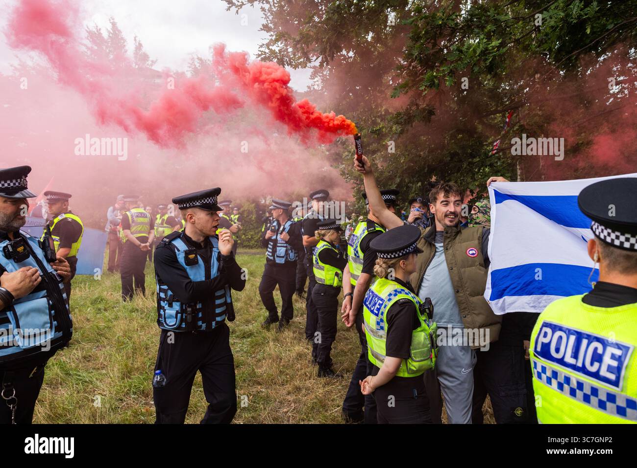 Leeds, UK. 01 AUG, 2025. Man holds red smoke flare next to Israeli flag ...
