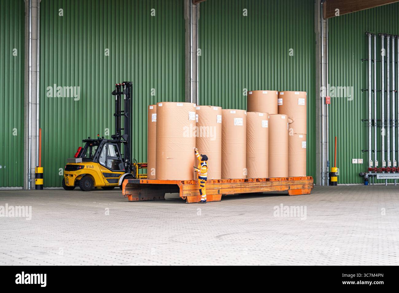 Worker Securing Large Paper Rolls on a Flatbed Trailer in a Warehouse ...