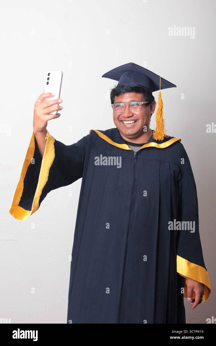 Young man dressed in cap and gown to celebrate his graduation uses his ...