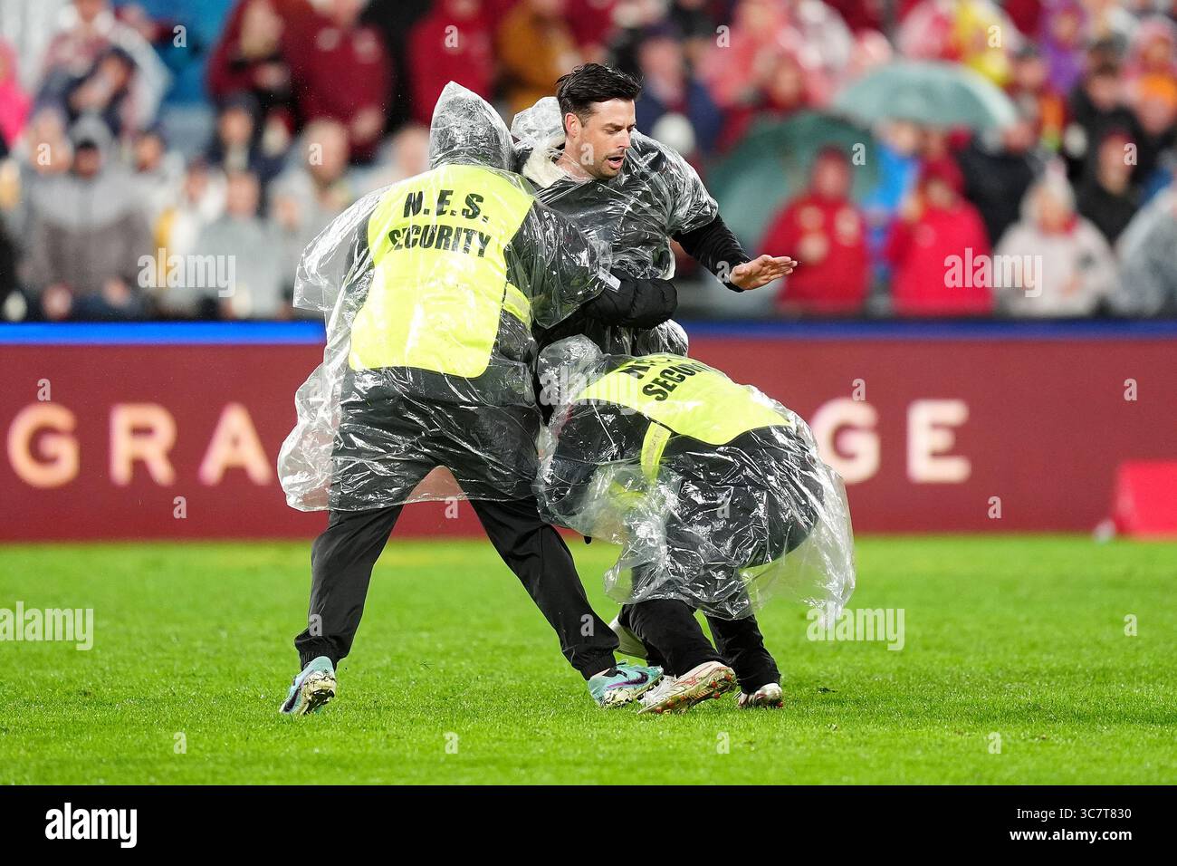 A pitch invader is apprehended by stadium security staff while play is ...