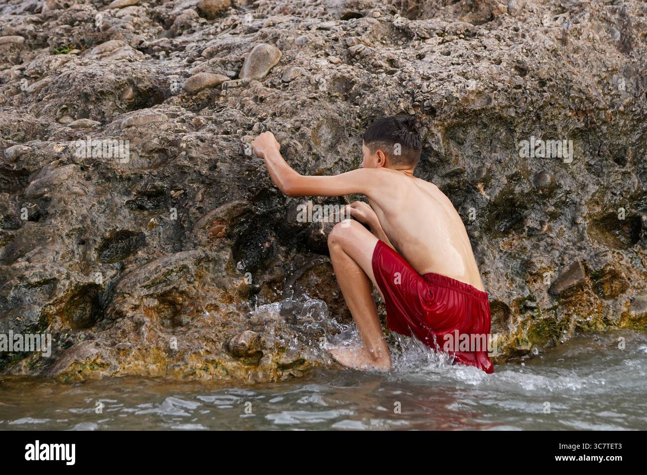 A boy climbs a rock in the Khabur river in the Kurdistan region.. A ...