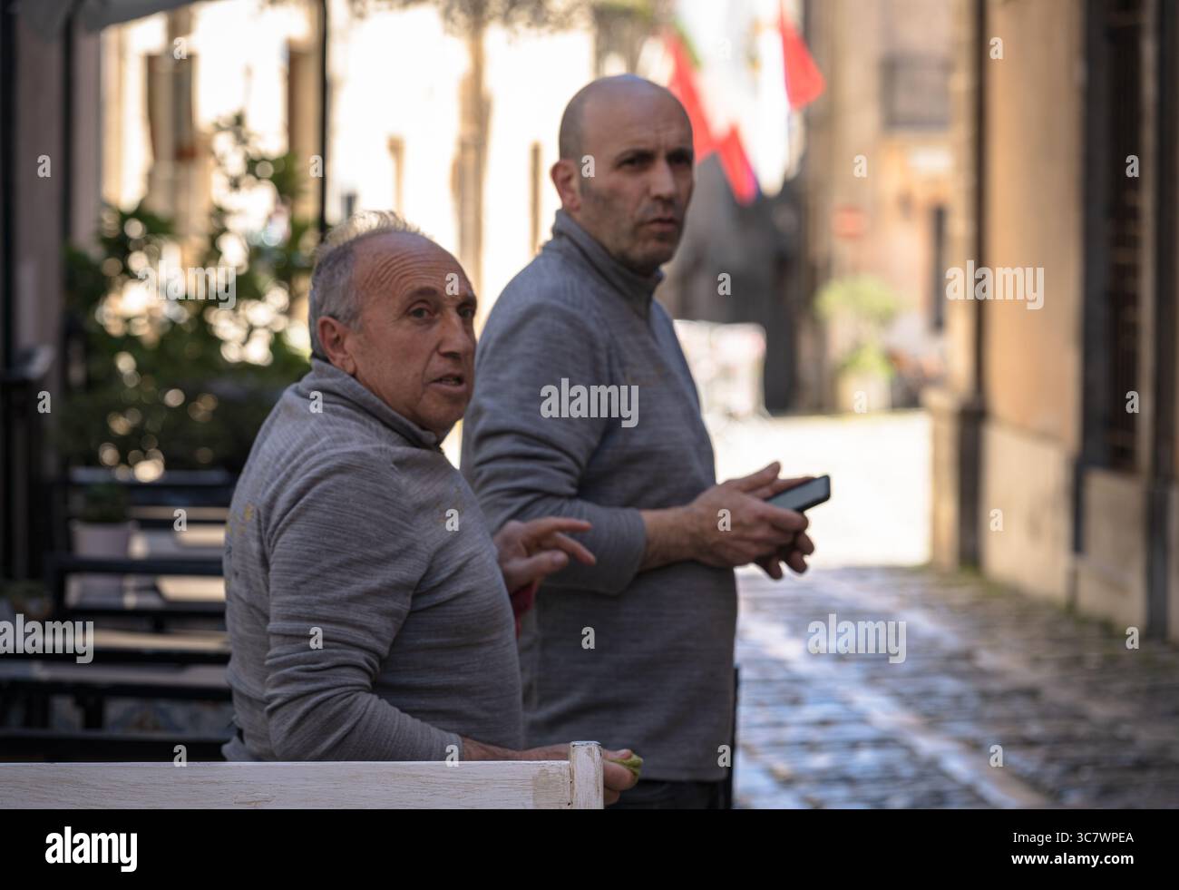 Sicily, Italy — May 2, 2025. Two men watch intently as a scene unfolds ...