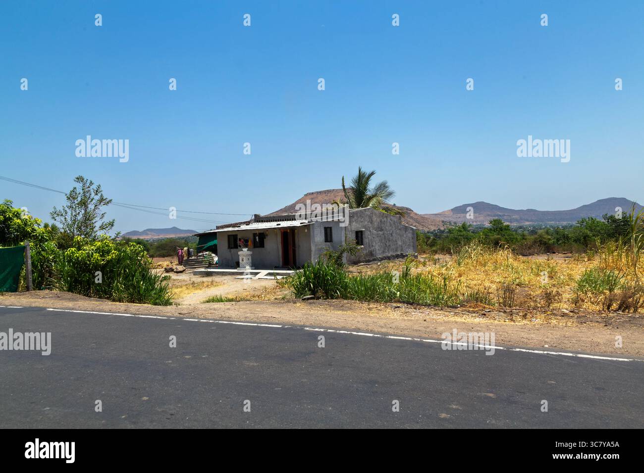 Rural Indian house along a countryside road with dry fields and distant ...