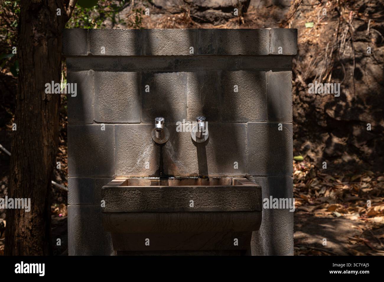 Old stone drinking water fountain with two metal taps, located outdoors ...