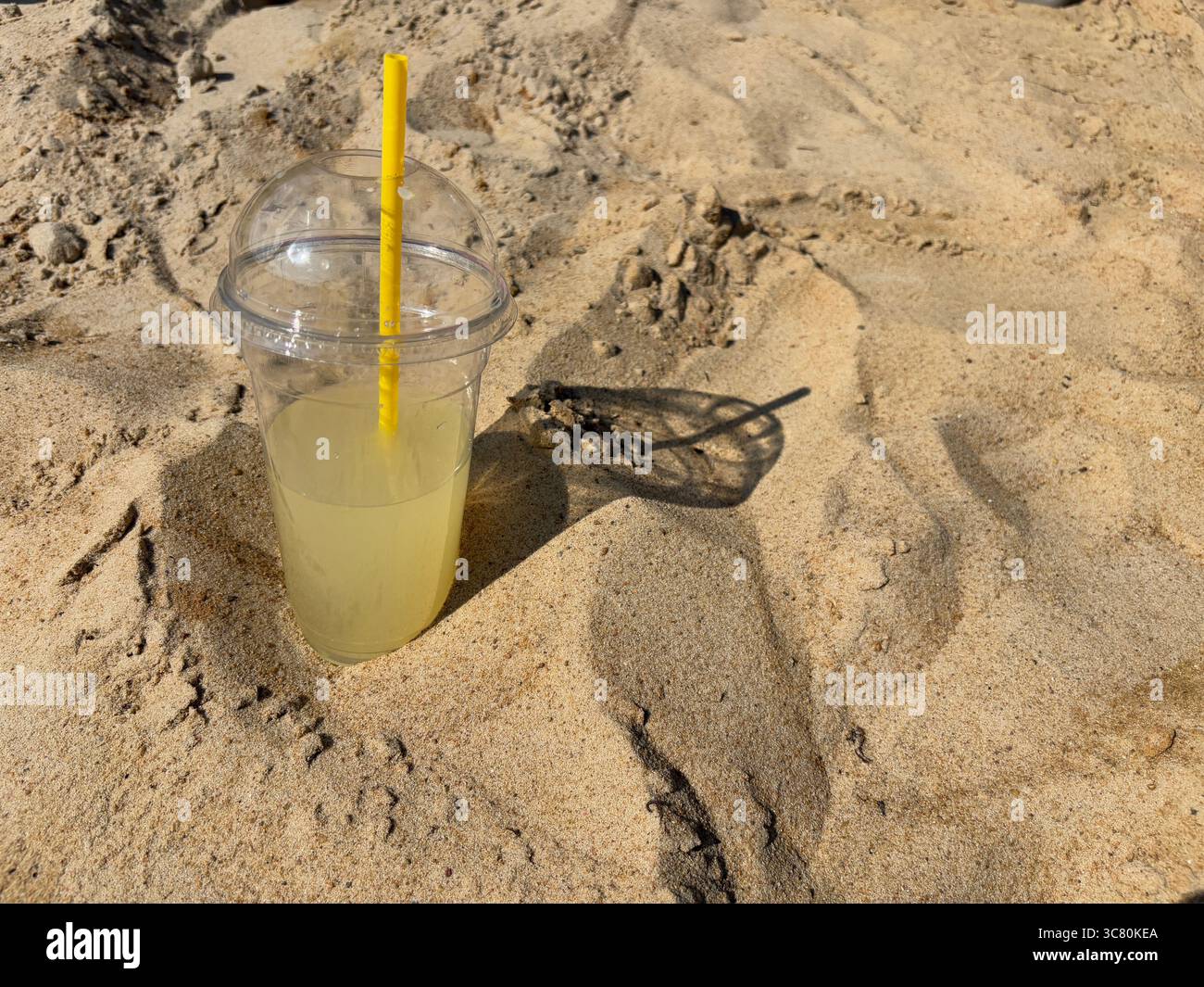 Plastic cup of lemonade with a yellow straw on sandy beach. Refreshing ...
