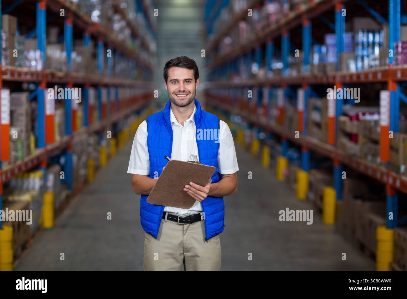 Warehouse worker checking stock levels on shelving racks in aisle ...