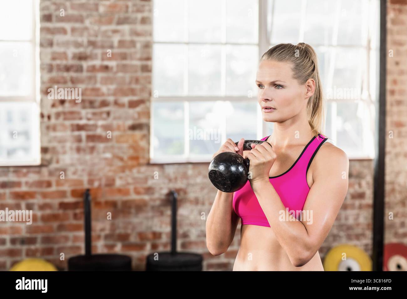 Fit woman is lifting black kettlebell at chest level near industrial ...