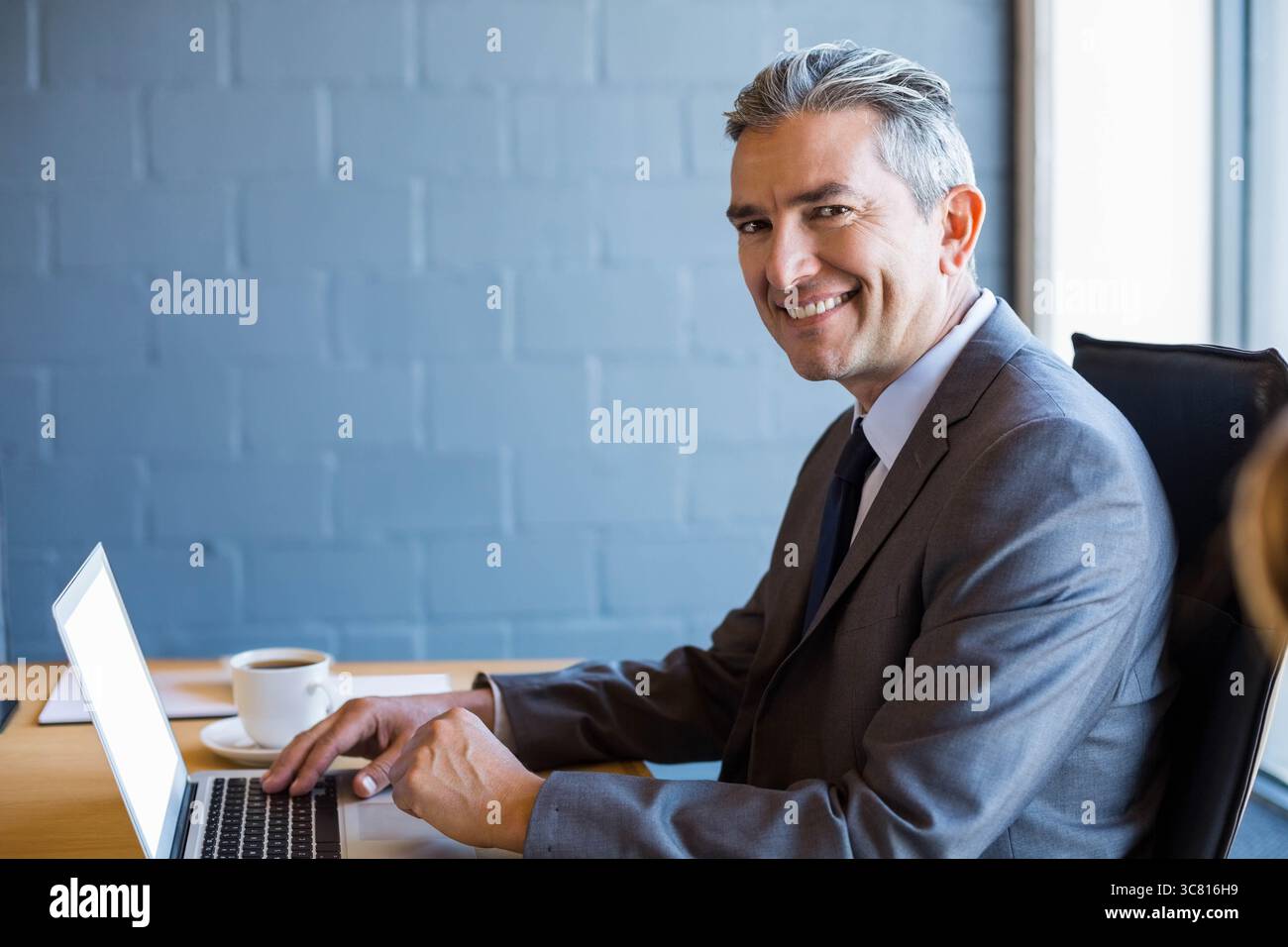 Laptop resting on wooden desk against light blue brick wall with coffee ...